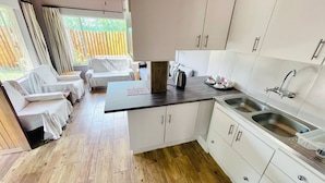 Uma cozinha moderna com armários brancos, bancada preta e uma pia. Há uma área de refeições com cadeiras brancas e uma mesa.
