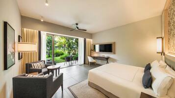 Quarto de hotel com cama, escrivaninha, cadeira, televisão e vista para um jardim.