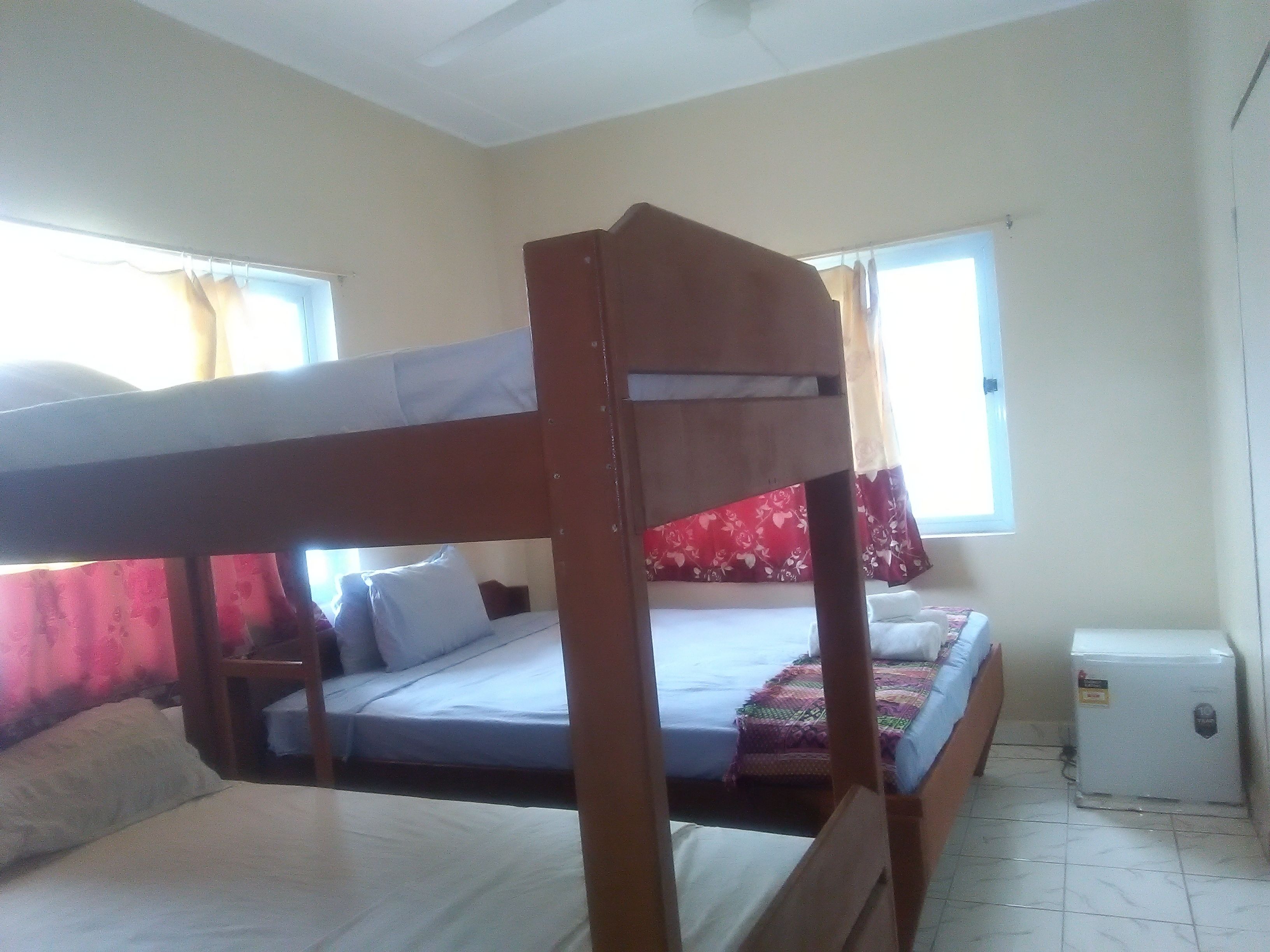 Quarto com beliche, uma pequena geladeira e janela com cortinas.