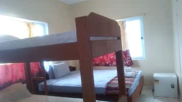 Quarto com beliche, uma pequena geladeira e janela com cortinas.