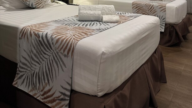 Quarto de hotel com duas camas, uma grande obra de arte vegetal na parede, uma cadeira suspensa e uma escada.
