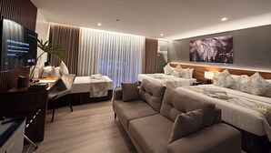 Quarto de hotel moderno com uma cama grande, um sofá, uma TV e uma escrivaninha.