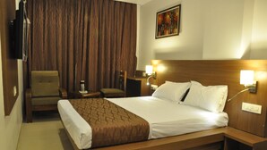 Quarto de hotel com cama, cadeira, escrivaninha e televisão fixada na parede.