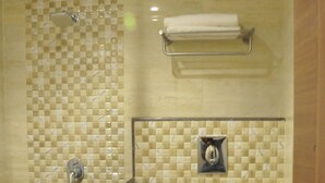 Um banheiro com parede de azulejos xadrez, vaso sanitário, chuveiro e porta-toalhas.