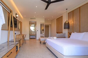 Quarto de hotel com uma cama, uma escrivaninha, uma cadeira, um ventilador de teto e um lustre.