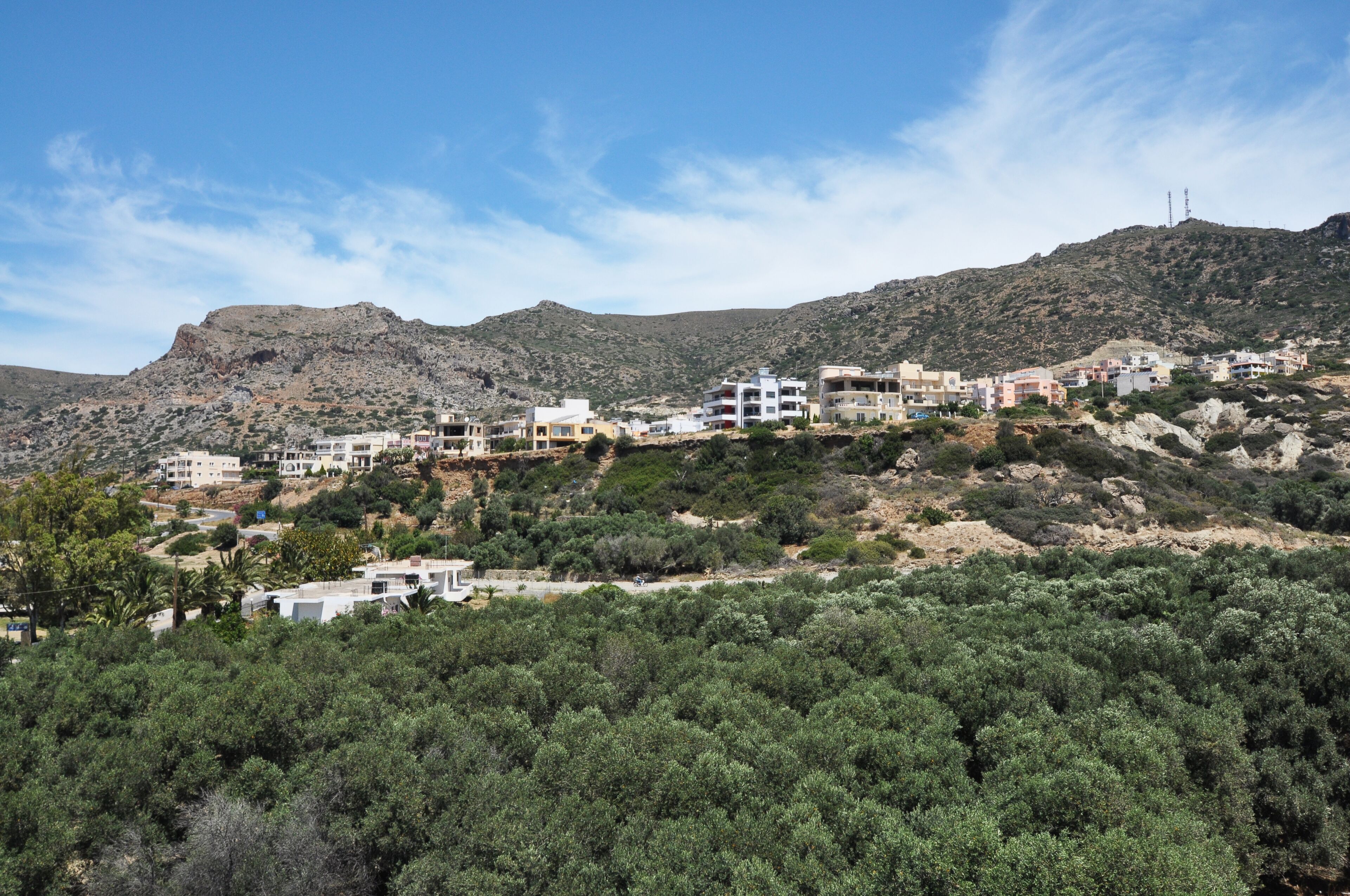 Um povoado em encosta, com construções, vegetação densa e montanhas ao fundo.