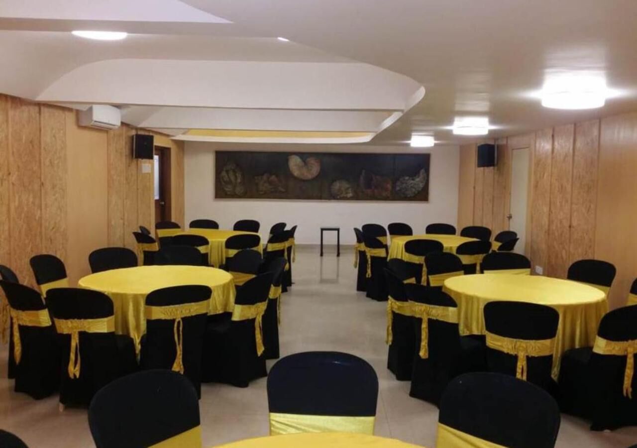 Uma sala de conferências com várias mesas redondas e cadeiras pretas, cada uma com toalha amarela.
