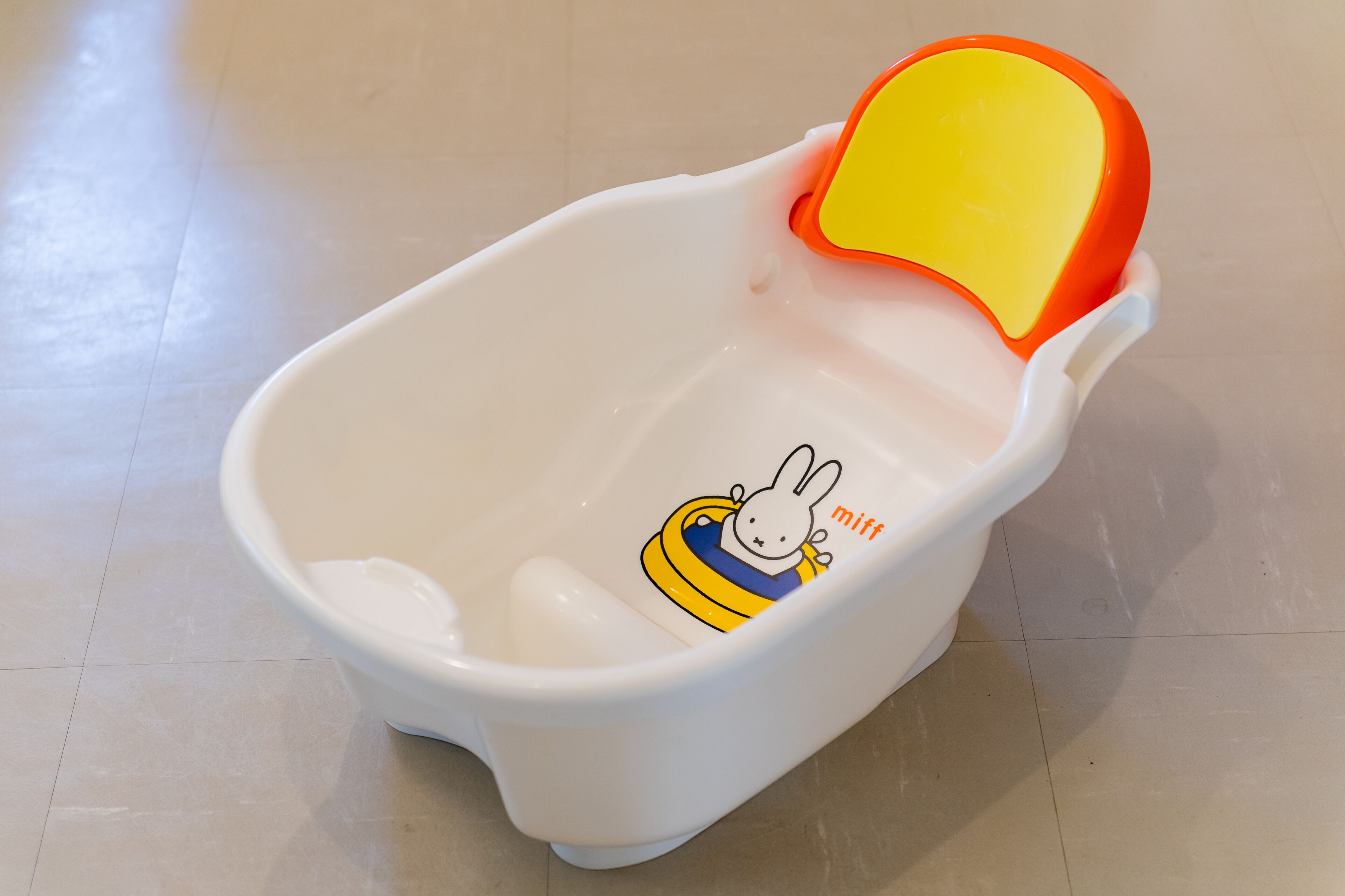 Uma banheira branca para bebê com desenho de um coelho de desenho animado e um assento amarelo e laranja.
