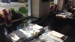 Mesa de jantar posta com copos de vinho, talheres e um pequeno vaso com flores.