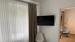 Quarto de hotel moderno com uma cama, uma TV de tela plana na parede, uma cadeira branca e piso de madeira.