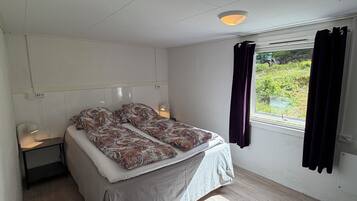 Quarto com cama, abajures, janela com cortinas e vista para o verde lá fora.