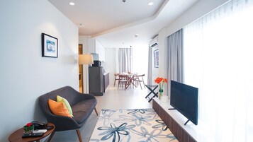 Uma sala de estar moderna com sofá, televisão e uma área de jantar ao fundo.