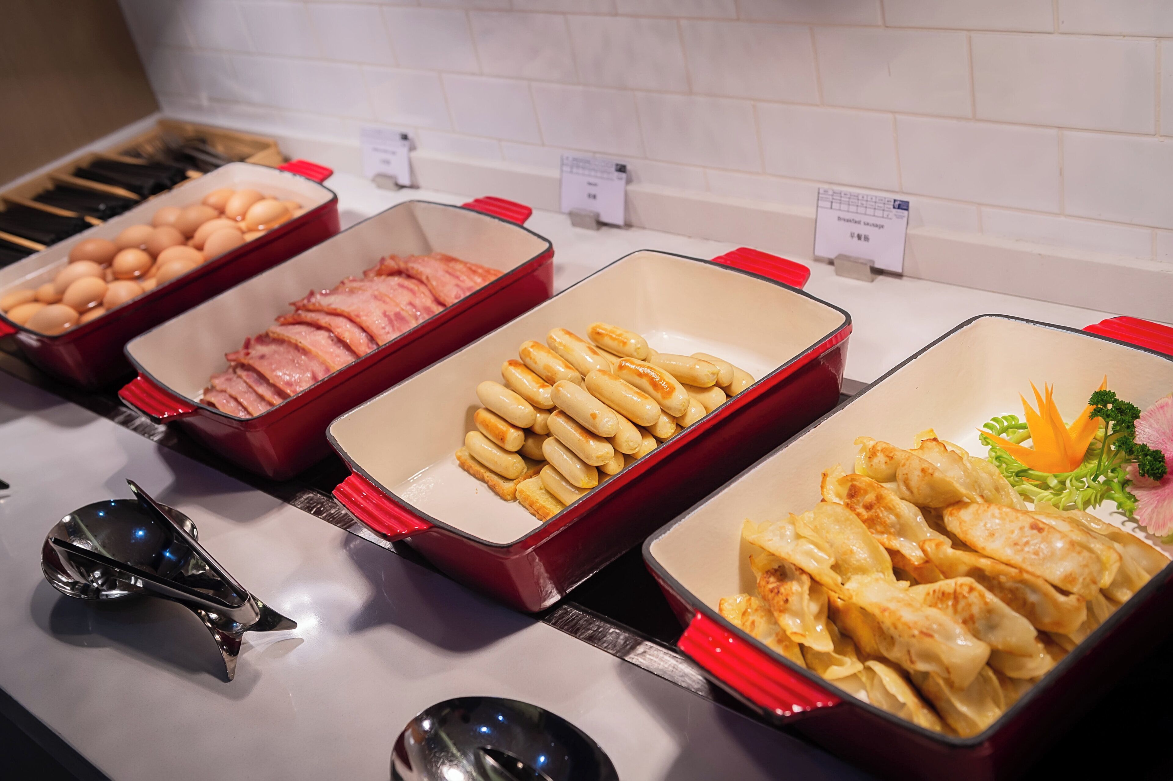 Buffet com diversos alimentos, incluindo ovos, presunto, salsichas e dumplings.