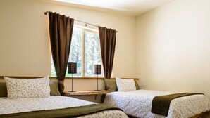 Quarto com duas camas, uma janela com cortinas, uma mesa pequena e um abajur.