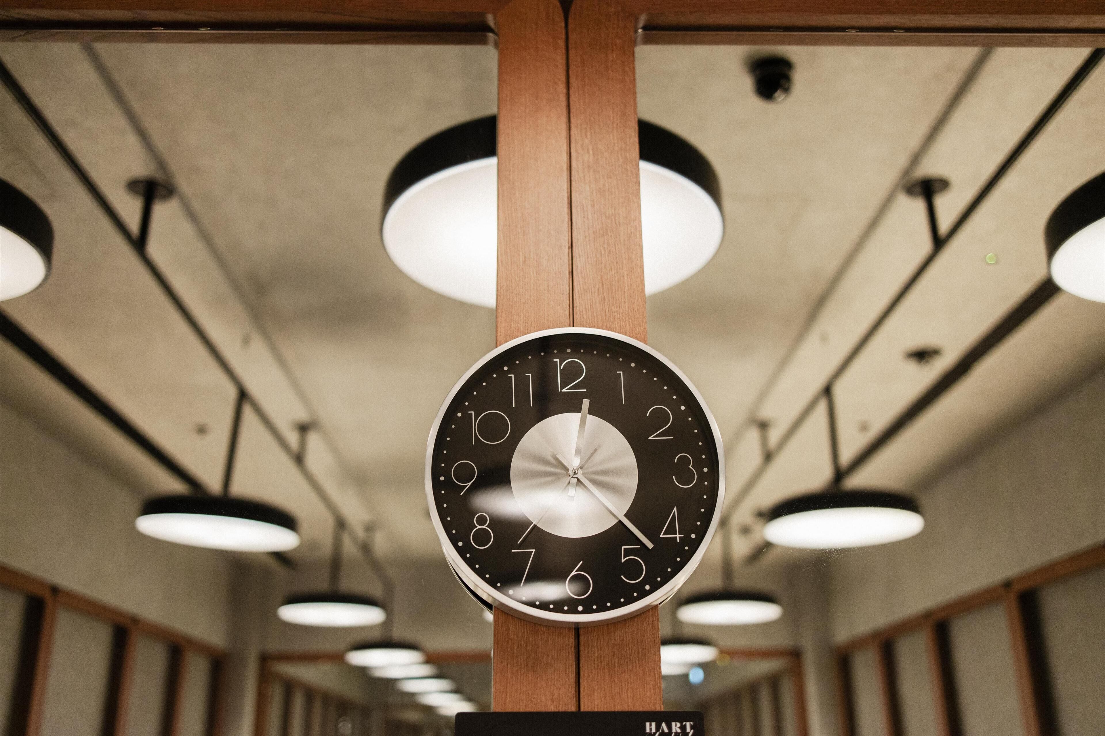Um relógio fixado em um poste de madeira em um corredor com várias luminárias no teto.