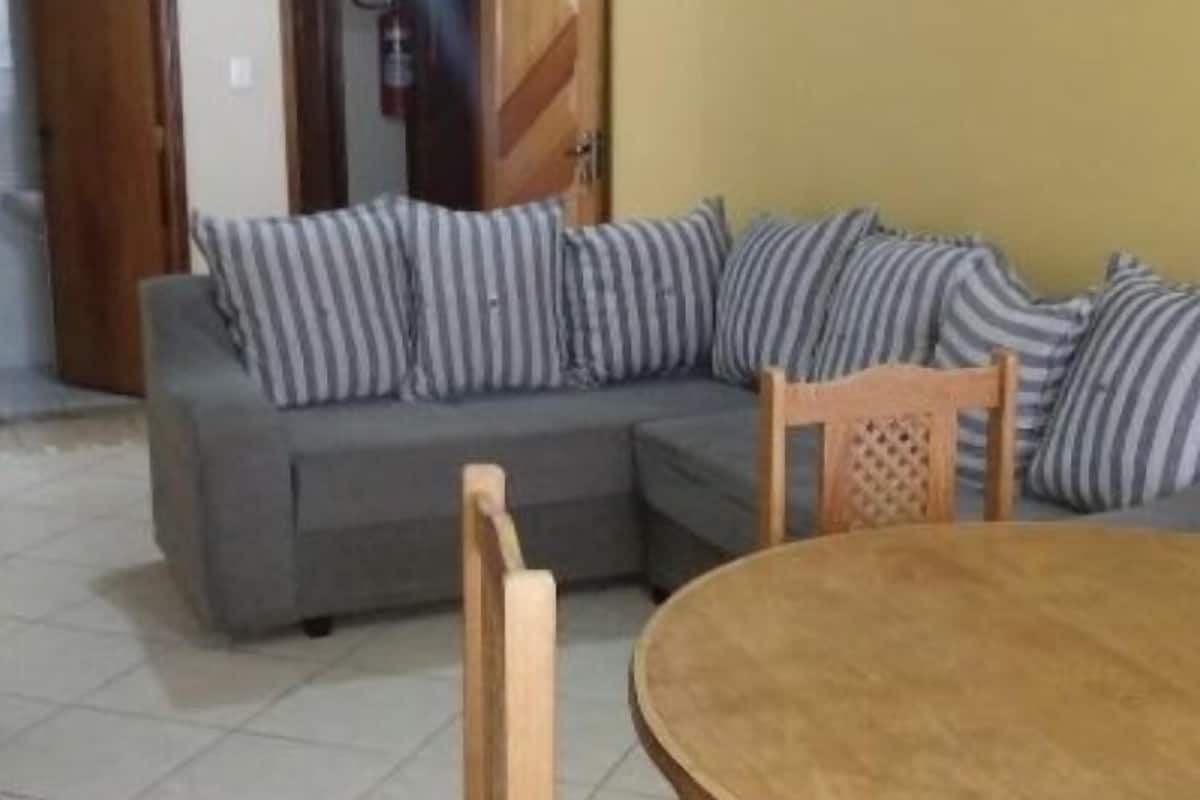 Uma sala de estar com um sofá cinzento, almofadas listradas, uma mesa de jantar de madeira e cadeiras.