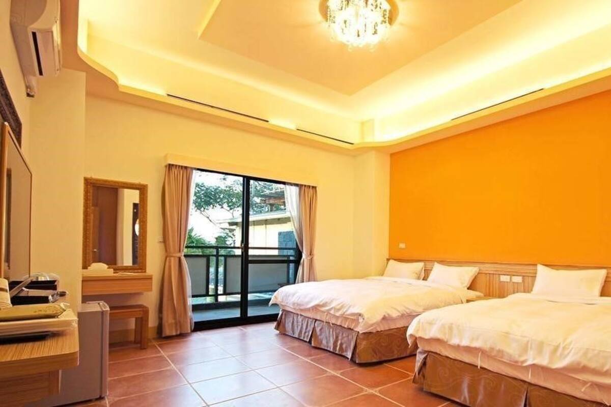 Quarto de hotel com duas camas, varanda, escrivaninha com cadeira e uma janela grande.