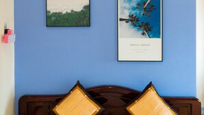 Quarto com parede azul, duas imagens emolduradas, cama com cabeceira de madeira e um objeto rosa na parede.