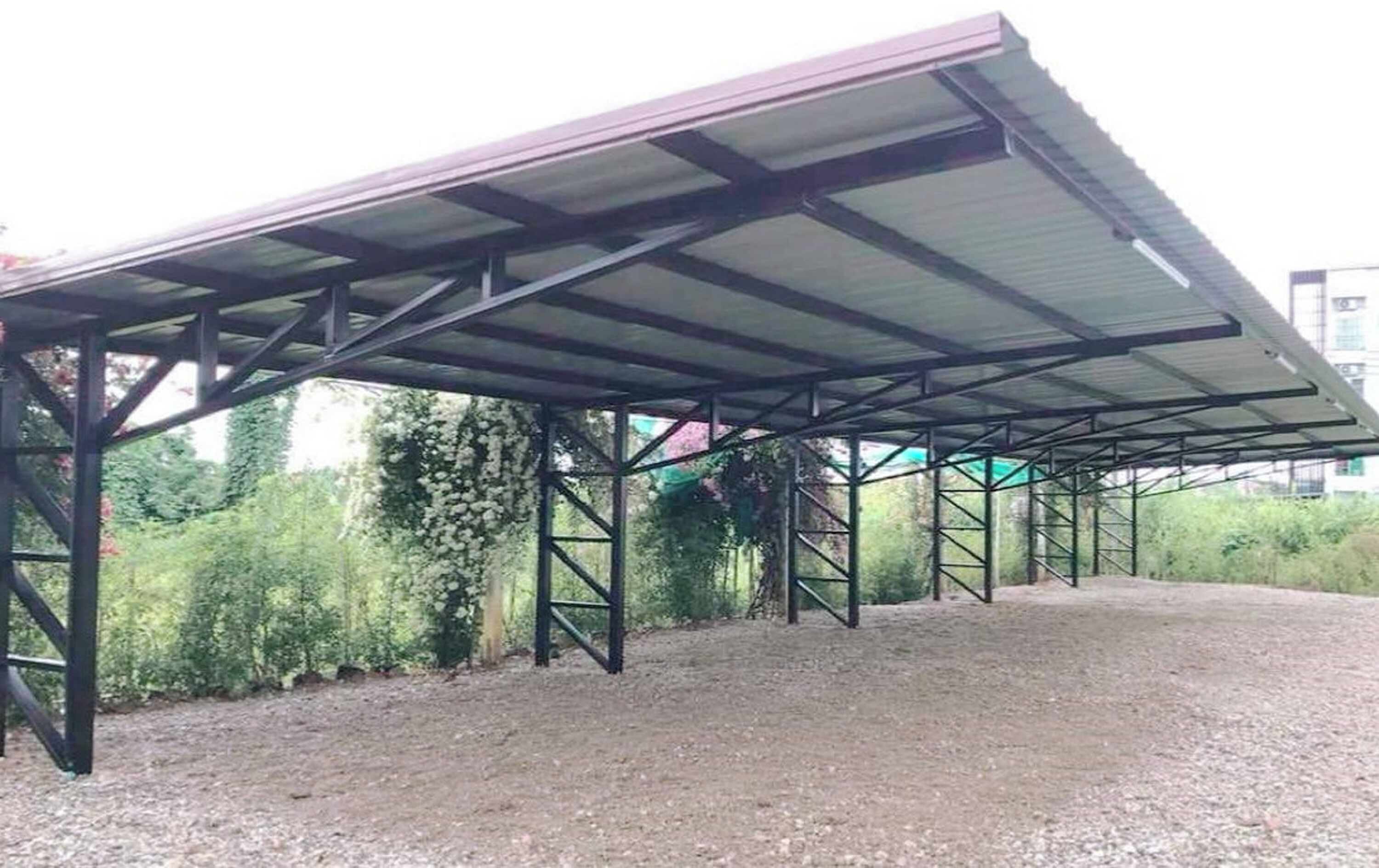 Uma área externa coberta com telhado de metal e chão de cascalho, rodeada por vegetação.