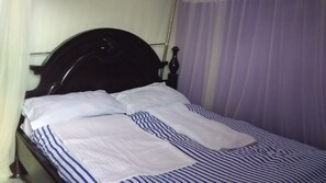 Uma cama com cabeceira escura, almofadas brancas e roupa de cama listrada.