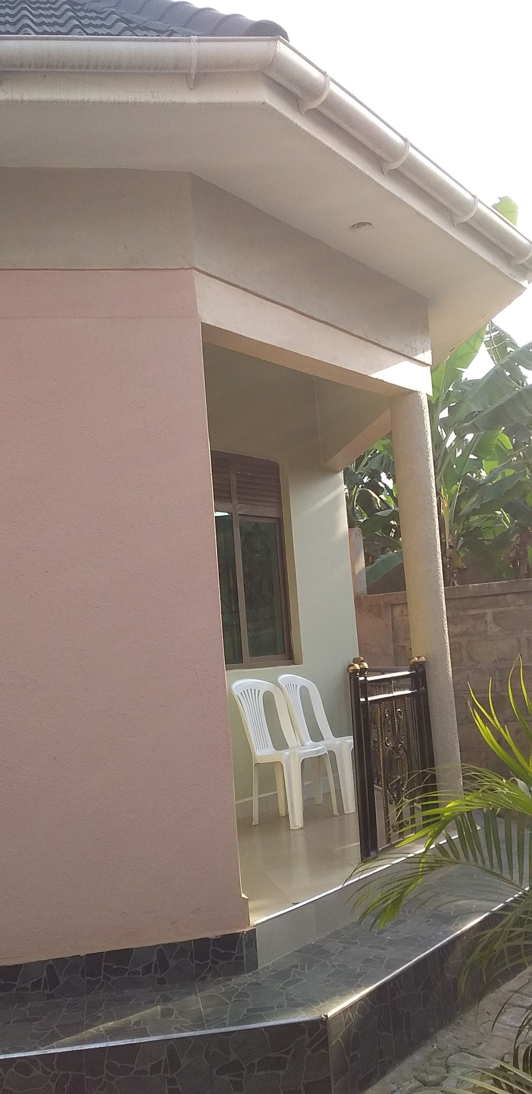 Um edifício com fachada rosa, um alpendre coberto com duas cadeiras de plástico brancas e um portão preto.