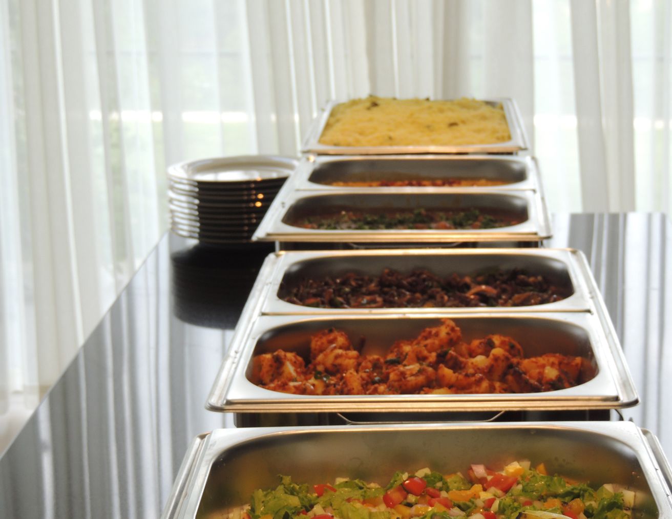 Buffet com diversos pratos em bandejas de metal.