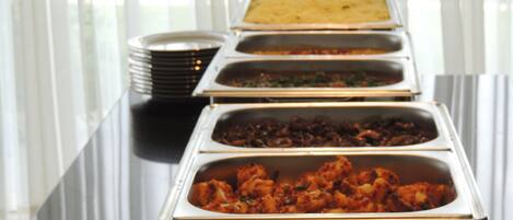 Buffet com diversos pratos em bandejas de metal.