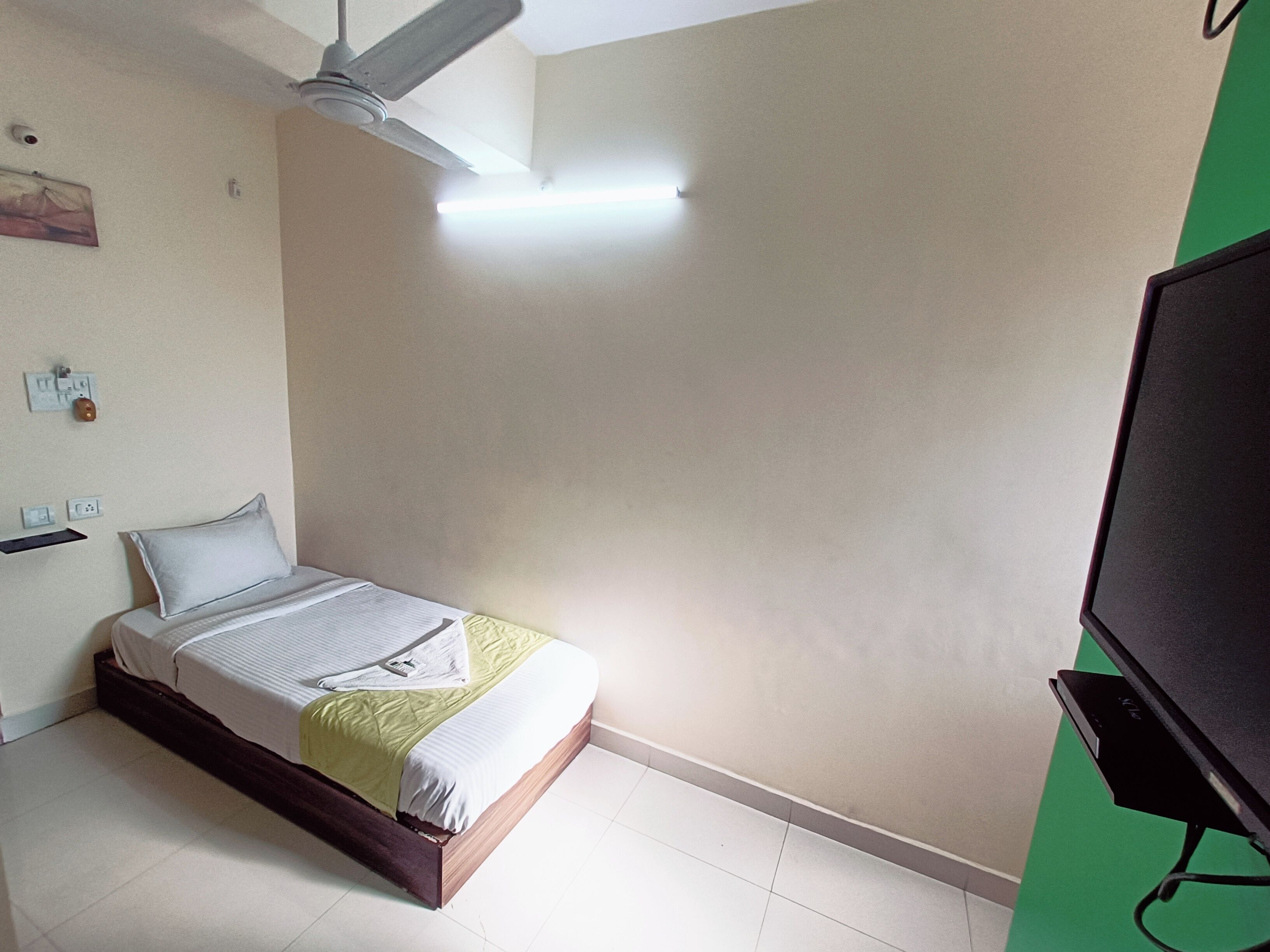 Quarto com cama, ventilador de teto, televisão na parede e luminária.