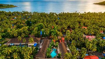 Vista aérea de um resort com piscina, cercado por palmeiras e edifícios com telhados vermelhos.