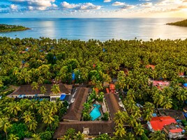 Vista aérea de um resort com piscina, cercado por palmeiras e edifícios com telhados vermelhos.