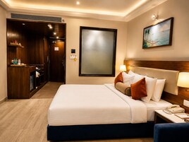 Quarto de hotel com cama, mesa de cabeceira, abajur e um quadro na parede.