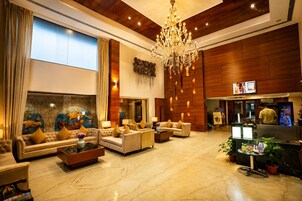 Um saguão de hotel com um candelabro, sofás, uma mesa de centro e um balcão de recepção.