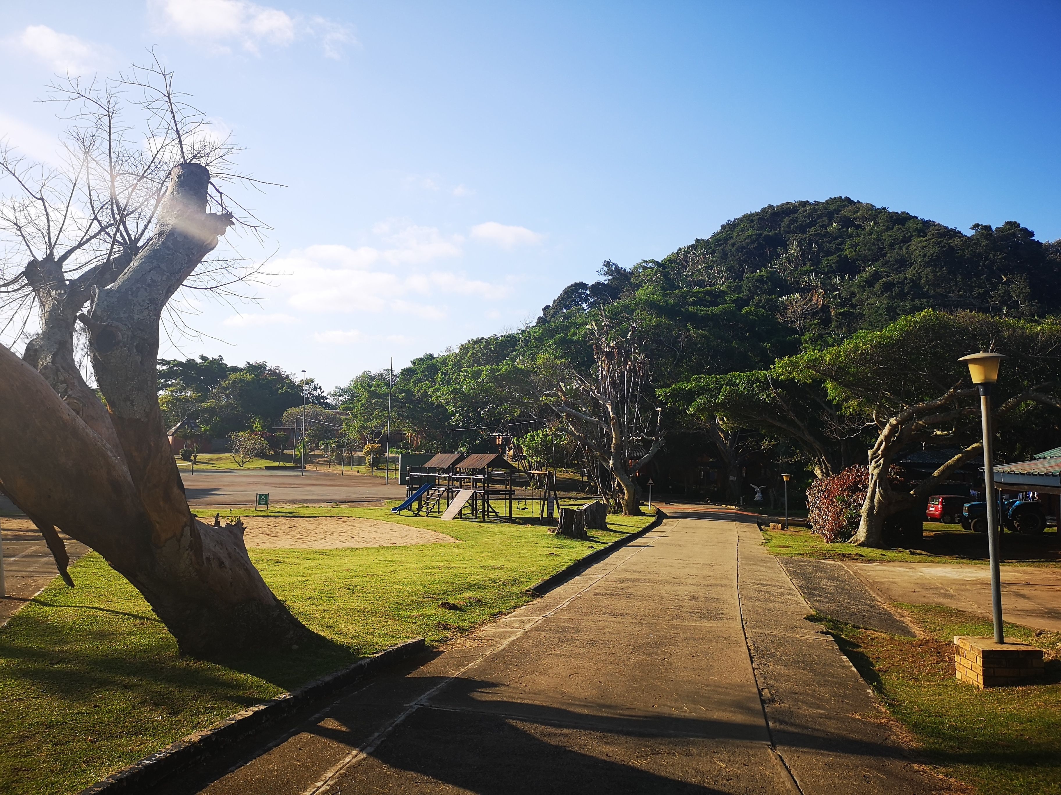 Um parque com um parquinho, uma trilha pavimentada e uma colina ao fundo.