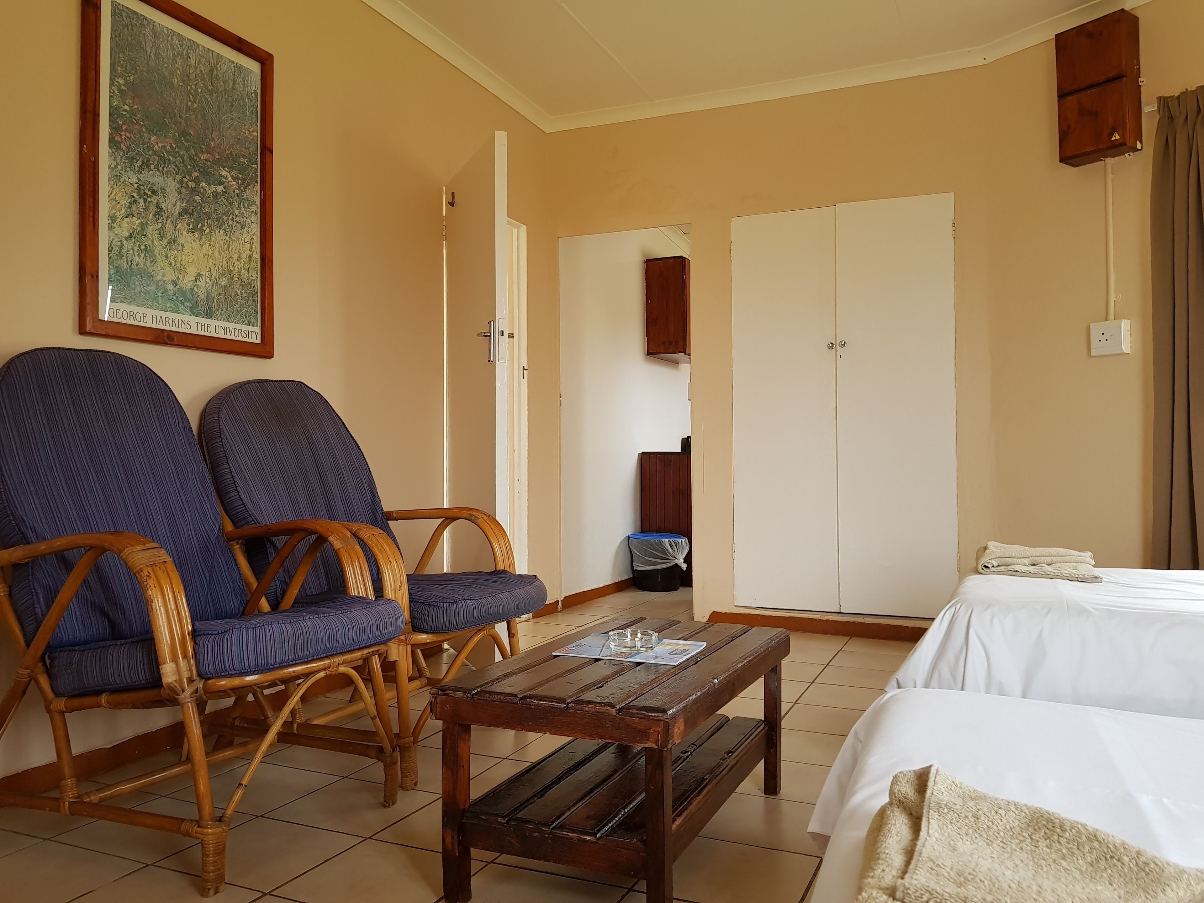 Um quarto com duas cadeiras de vime, uma mesa de centro de madeira, uma cama e um guarda-roupa.