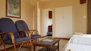 Um quarto com duas cadeiras de vime, uma mesa de centro de madeira, uma cama e um guarda-roupa.