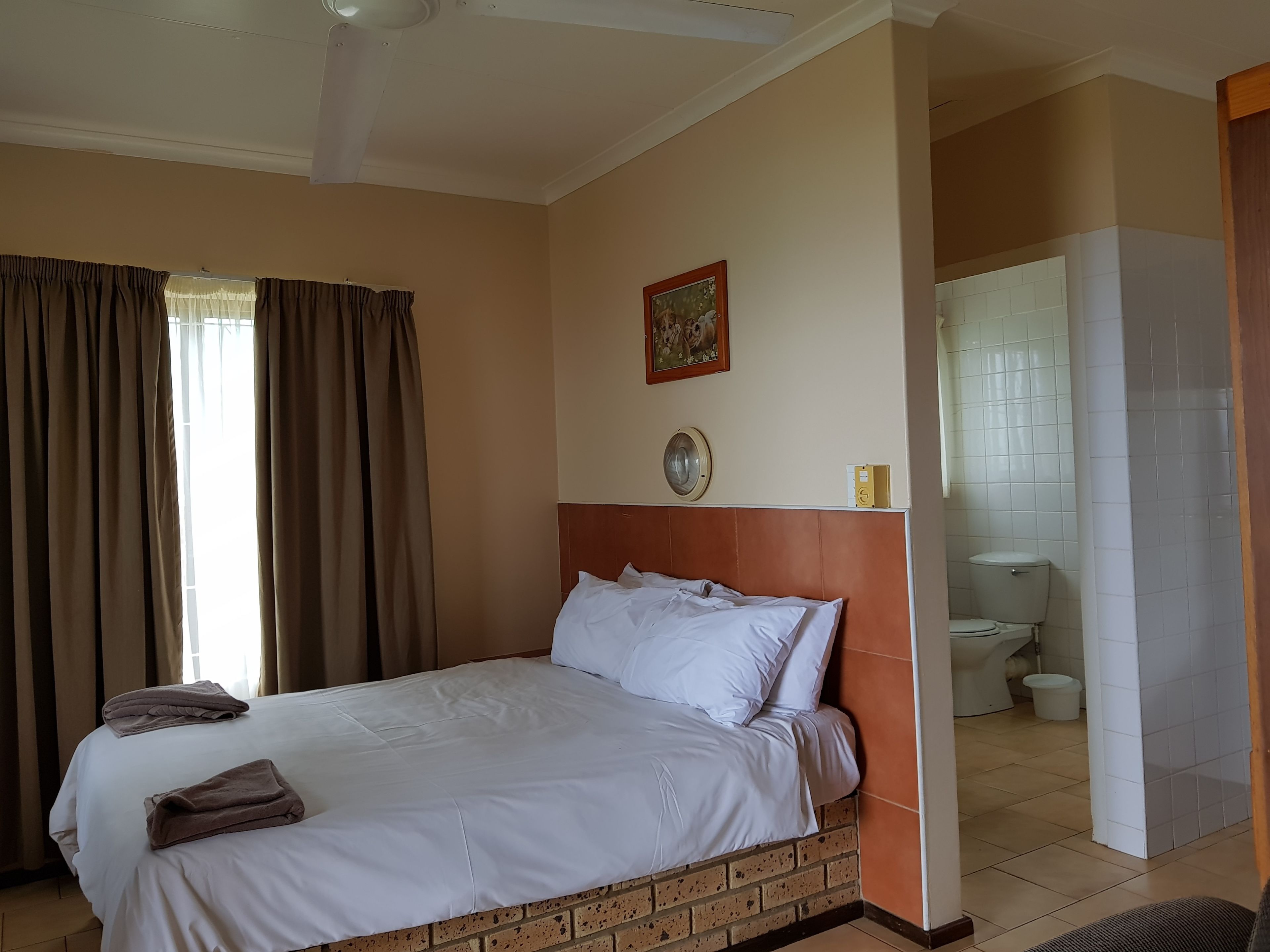 Quarto de hotel com cama, cortinas, um quadro, relógio e vista para o banheiro.