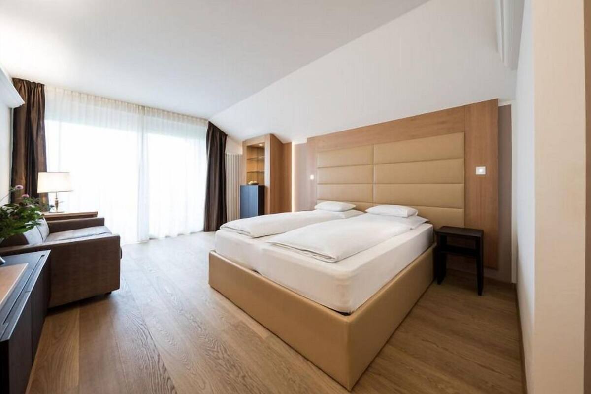 Quarto de hotel moderno com uma cama grande, piso de madeira, uma escrivaninha e uma pequena mesa lateral.