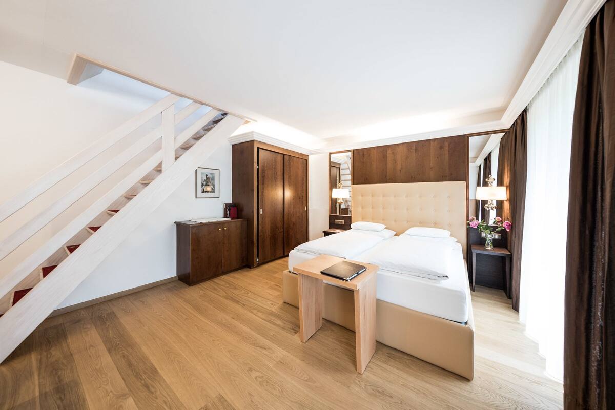 Quarto moderno com escada de madeira, cama, mesa de cabeceira e criado-mudo.