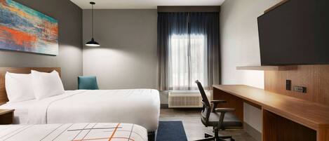 Quarto de hotel com duas camas, uma escrivaninha, uma cadeira, televisão e uma janela grande com cortinas.