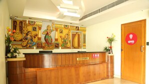 Uma mesa de recepção com uma placa 'RECEPTION', uma porta de madeira com o logotipo 'YOYO' e uma parede com obras de arte culturais.