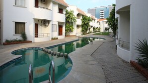 Uma área de piscina com superfície de água límpida, rodeada por edifícios brancos com varandas e telhados de telhas vermelhas.