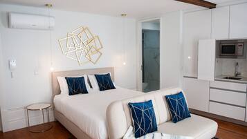 Quarto moderno com uma cama grande, uma mesinha de cabeceira, televisão integrada e uma área de cozinha com micro-ondas.