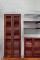 Quarto com guarda-roupa de madeira, um pequeno armário e estante.