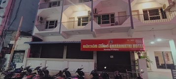 Hotel com placa vermelha, varandas e scooters estacionadas.
