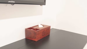 Quarto com uma mesa preta, uma caixa vermelha e uma TV fixada na parede.