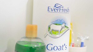 Uma prateleira no banheiro com uma garrafa de Shampoo Corporal de Leite de Cabra e uma garrafa de Bálsamo Jingle.