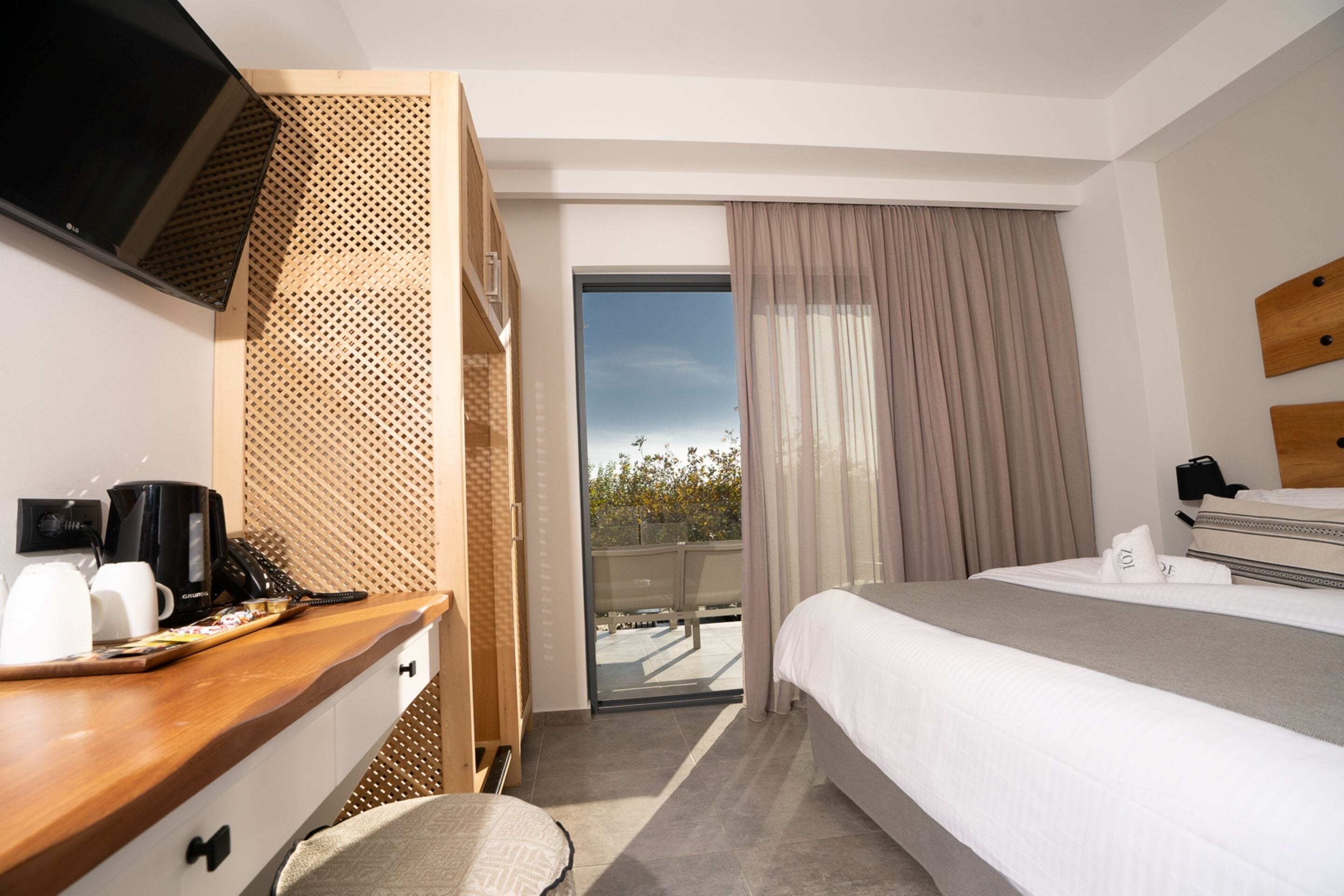 Quarto de hotel com cama, secretária com máquina de café, televisão e varanda com vista.