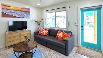 Uma sala de estar com sofá, televisão e uma pintura de pôr do sol.