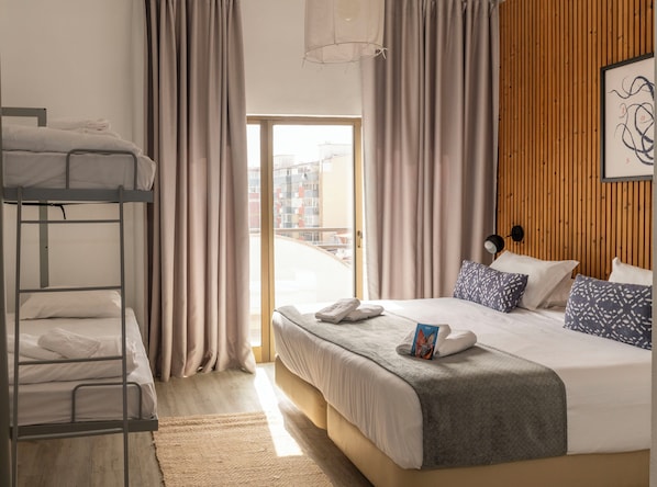 Quarto de hotel com cama beliche, uma cama de solteiro, vista através de uma porta de vidro e parede de madeira.