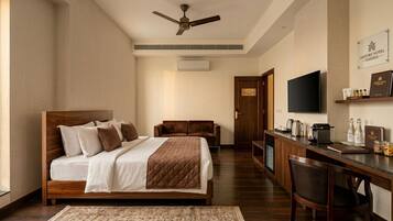 Quarto de hotel com cama, escrivaninha, televisão e ventoinha no teto.